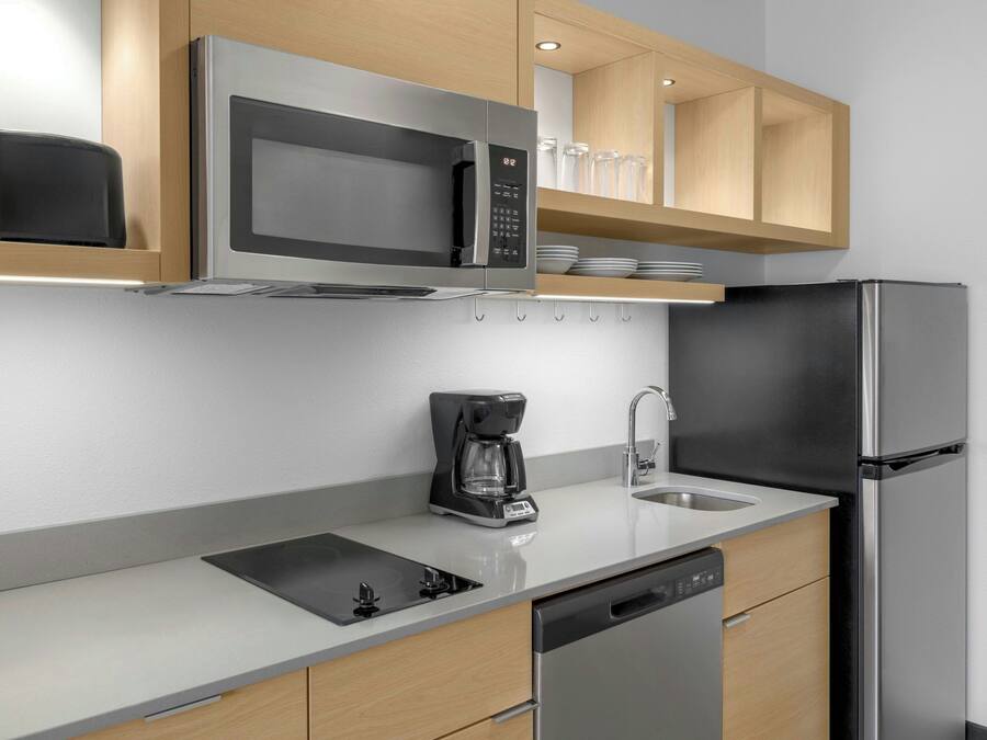 Uma cozinha moderna equipada com micro-ondas embutido, cafeteira, máquina de lavar louça e frigorífico em aço inoxidável.