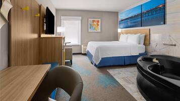 Quarto de hotel com cama, escrivaninha, cadeira, televisão, quadro e banheira.