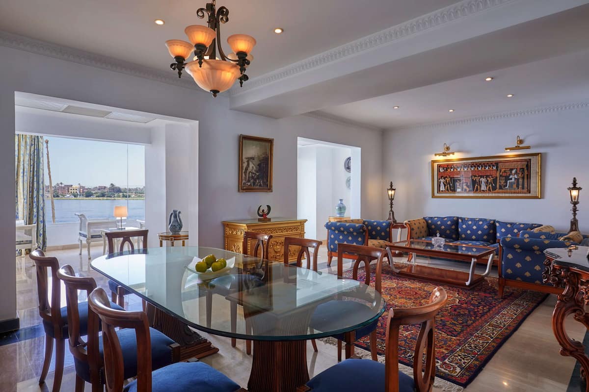Uma sala de estar ampla com mesa de jantar de vidro, sofás azuis e uma grande janela com vista para a cidade.