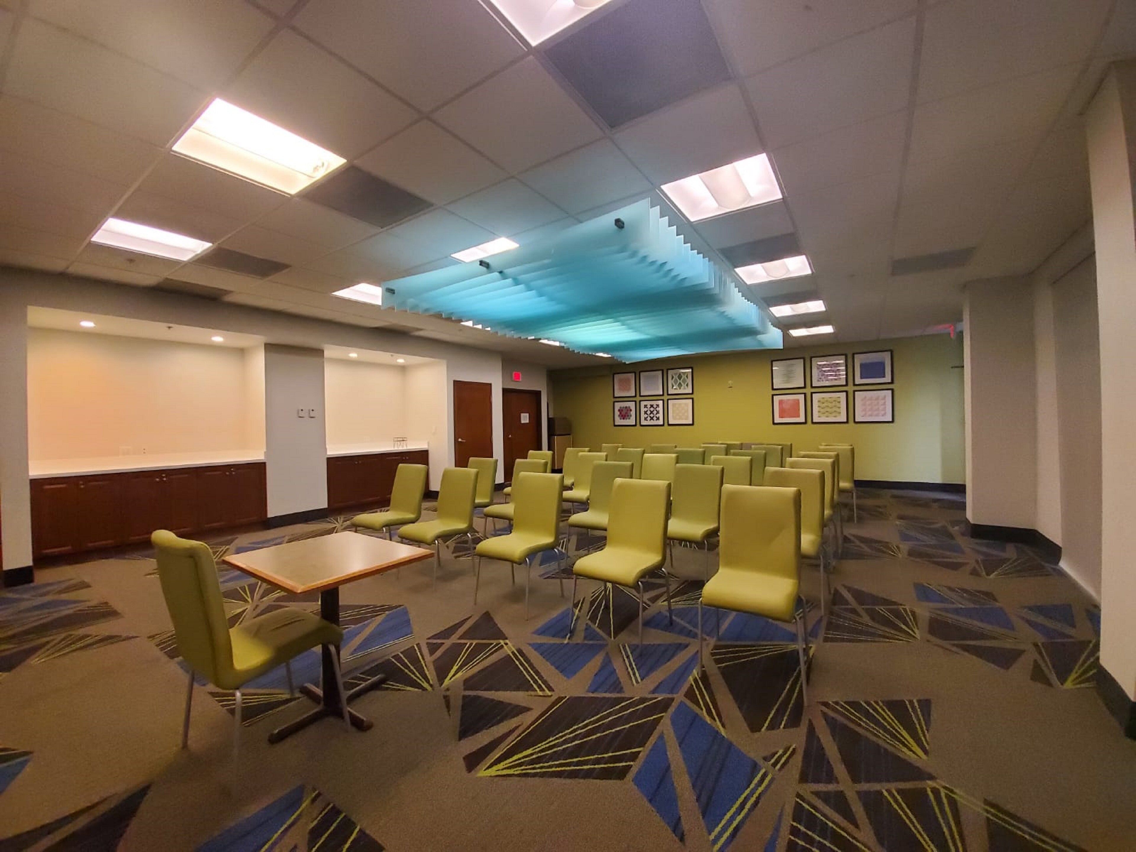 Sala de conferência com fileiras de cadeiras, uma tela de projetor e piso coberto de carpete.