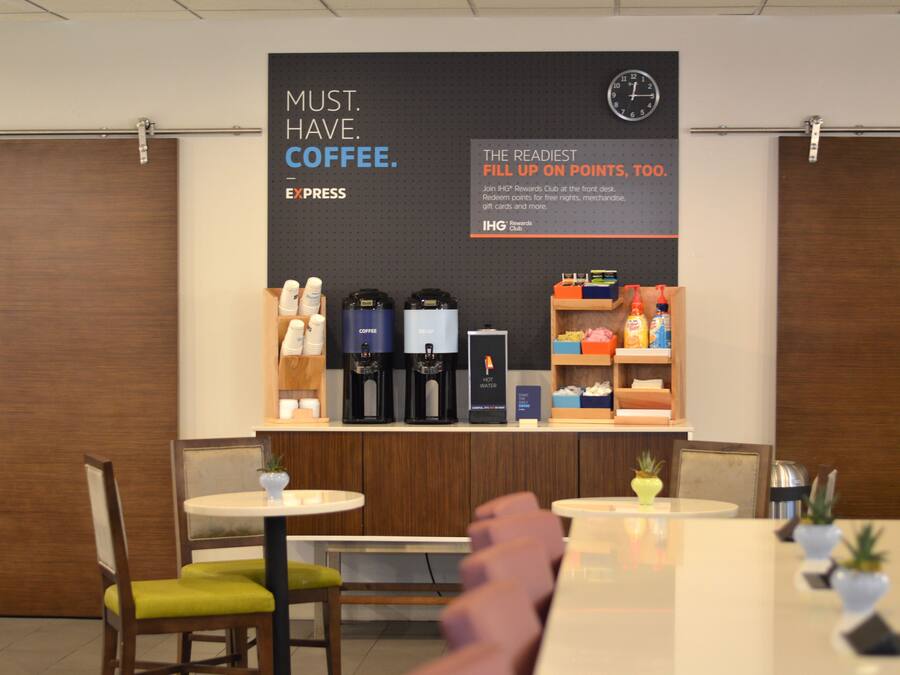 Uma estação de café com um aviso divulgando um programa de recompensas, um relógio e diversos dispensadores de café e água.