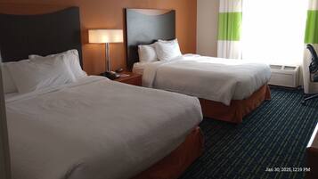 Quarto de hotel com duas camas, uma mesa de cabeceira com abajur, ar condicionado fixado na parede e uma janela com cortinas.