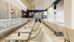 Restaurante moderno com mesas longas e cabines acolchoadas, teto decorativo e iluminação pendente.
