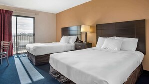 Quarto de hotel com duas camas, uma mesa de cabeceira, abajur, cadeira e vista para o exterior por uma porta de correr.