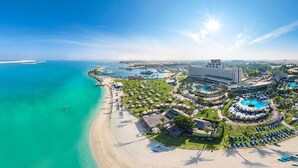 Um resort com uma praia, uma piscina grande e um prédio de hotel.