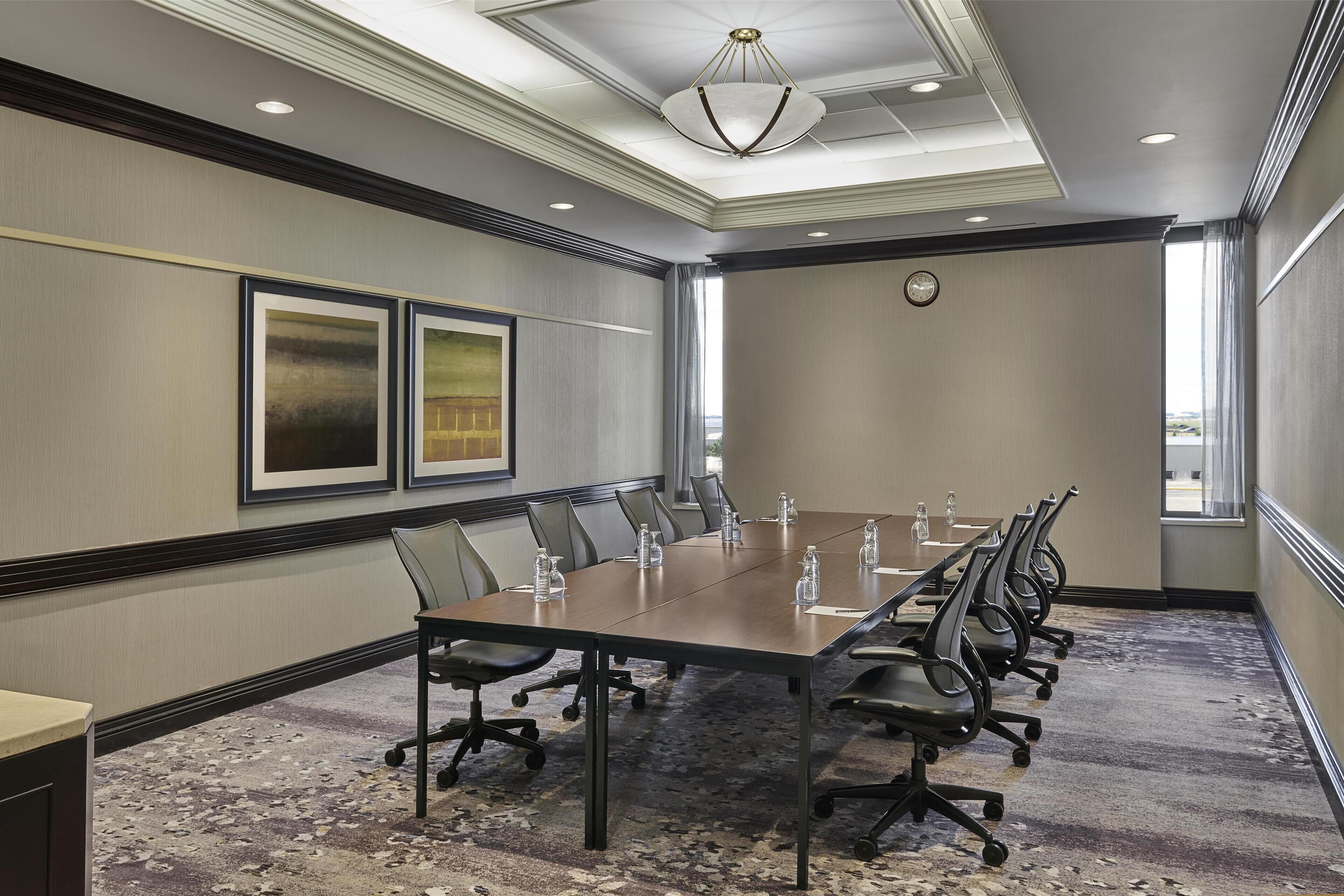 Uma sala de conferência com uma mesa comprida, cadeiras e um relógio na parede.