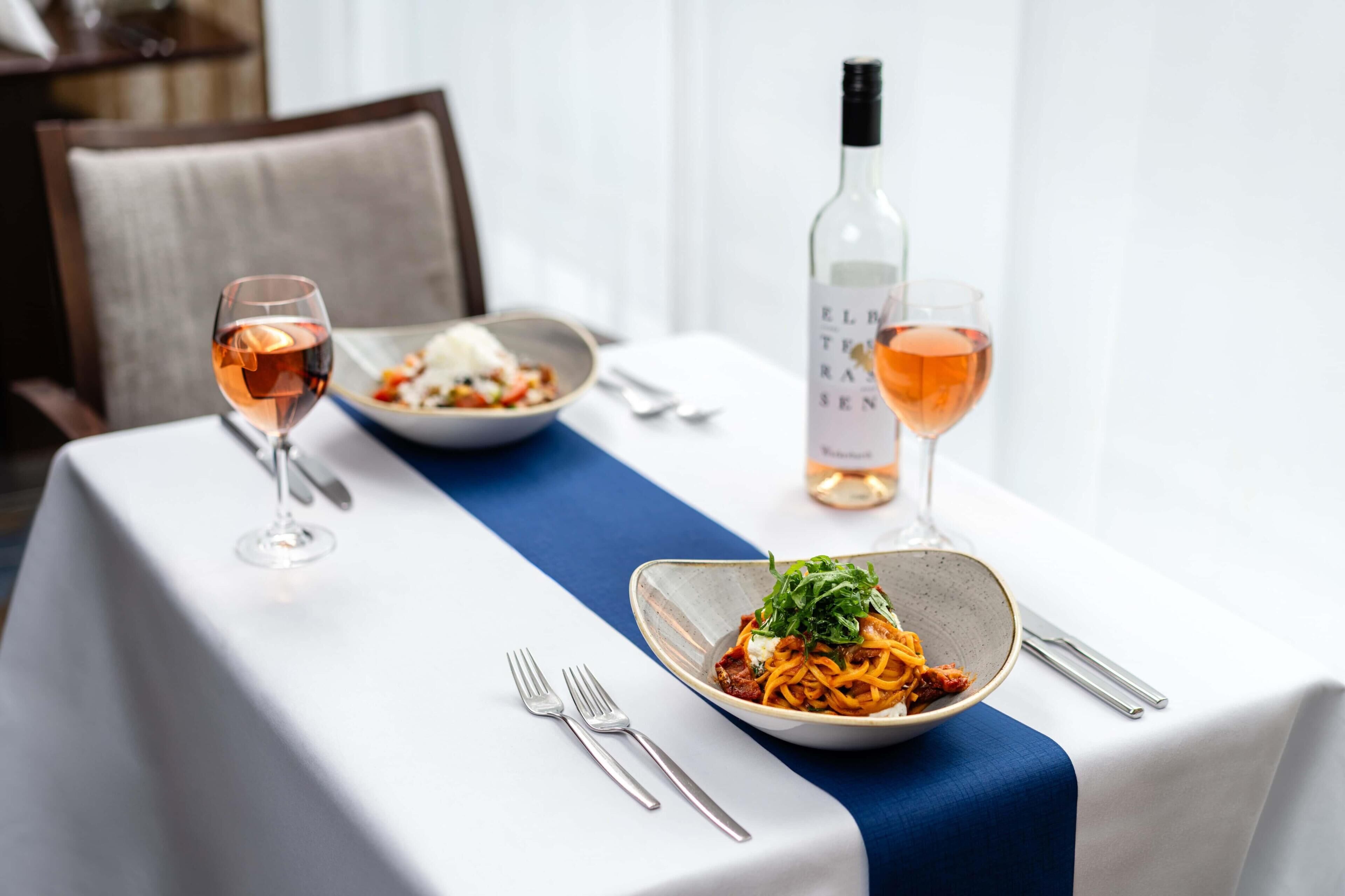 Uma mesa de jantar com dois pratos de comida, dois copos de vinho e uma garrafa de vinho.