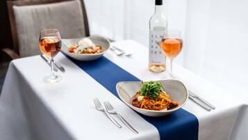 Uma mesa de jantar com dois pratos de comida, dois copos de vinho e uma garrafa de vinho.