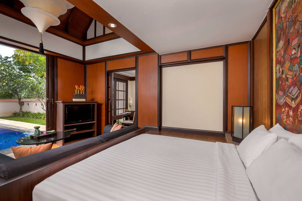 Quarto de hotel com uma cama grande, televisão, área de estar com vista para uma piscina e uma janela ampla.