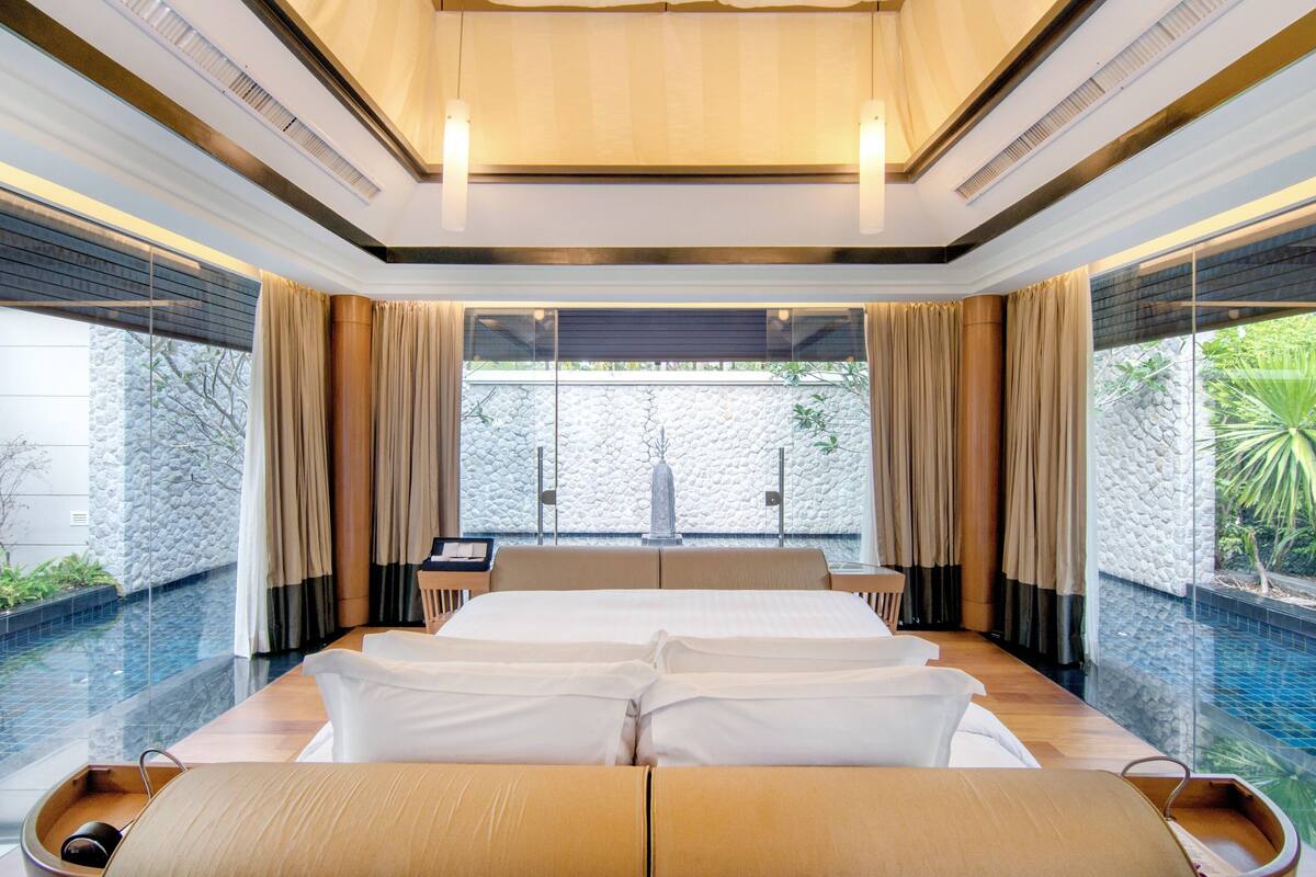 Quarto de hotel moderno com uma cama grande, vista para uma piscina e uma parede de pedra.