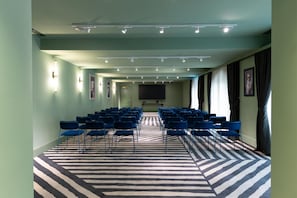 Uma sala de conferências com fileiras de cadeiras, carpete estampado e luminárias no teto.