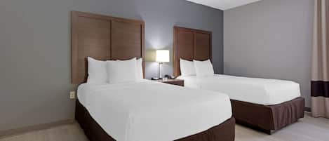 Quarto de hotel com duas camas, mesa de cabeceira, abajur e janela com cortinas.