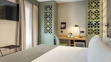 Quarto de hotel com uma cama, uma secretária com cadeira, uma televisão na parede e um minibar.