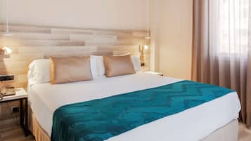 Quarto de hotel com uma cama grande, cabeceira de madeira, mesa de cabeceira com abajur e janela com cortinas.