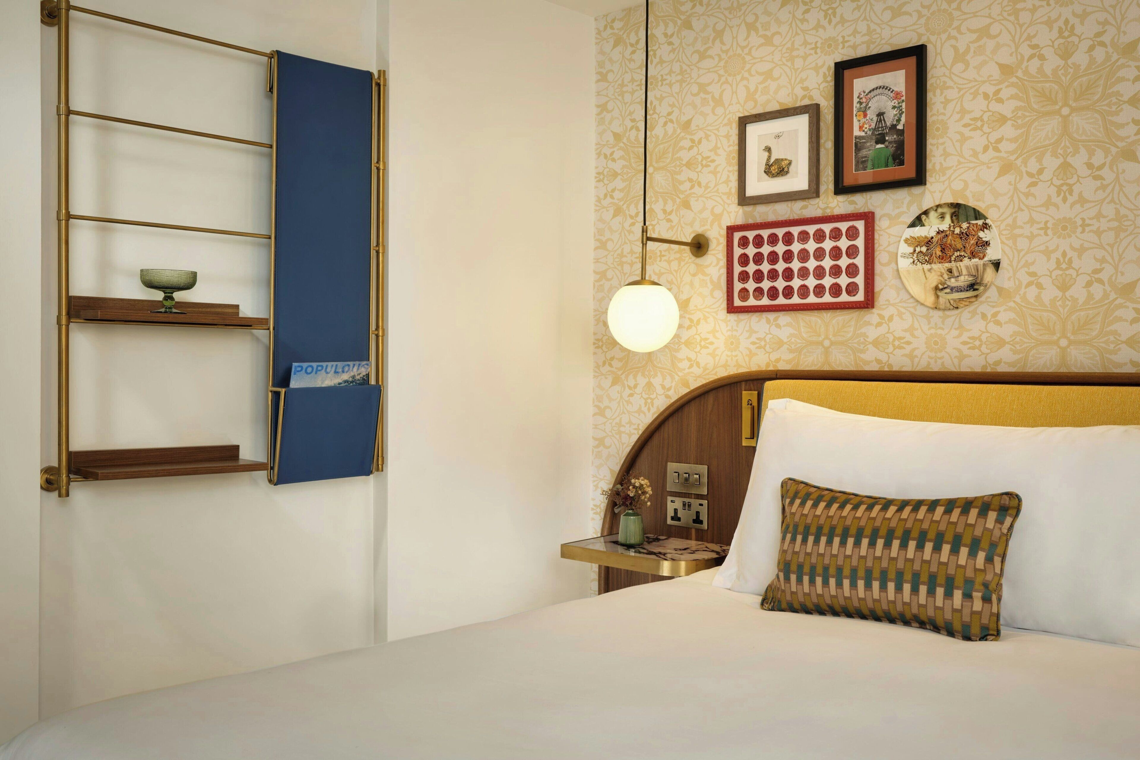 Quarto de hotel com cama, mesa de cabeceira, prateleira na parede com uma tigela, porta azul e arte decorativa na parede.