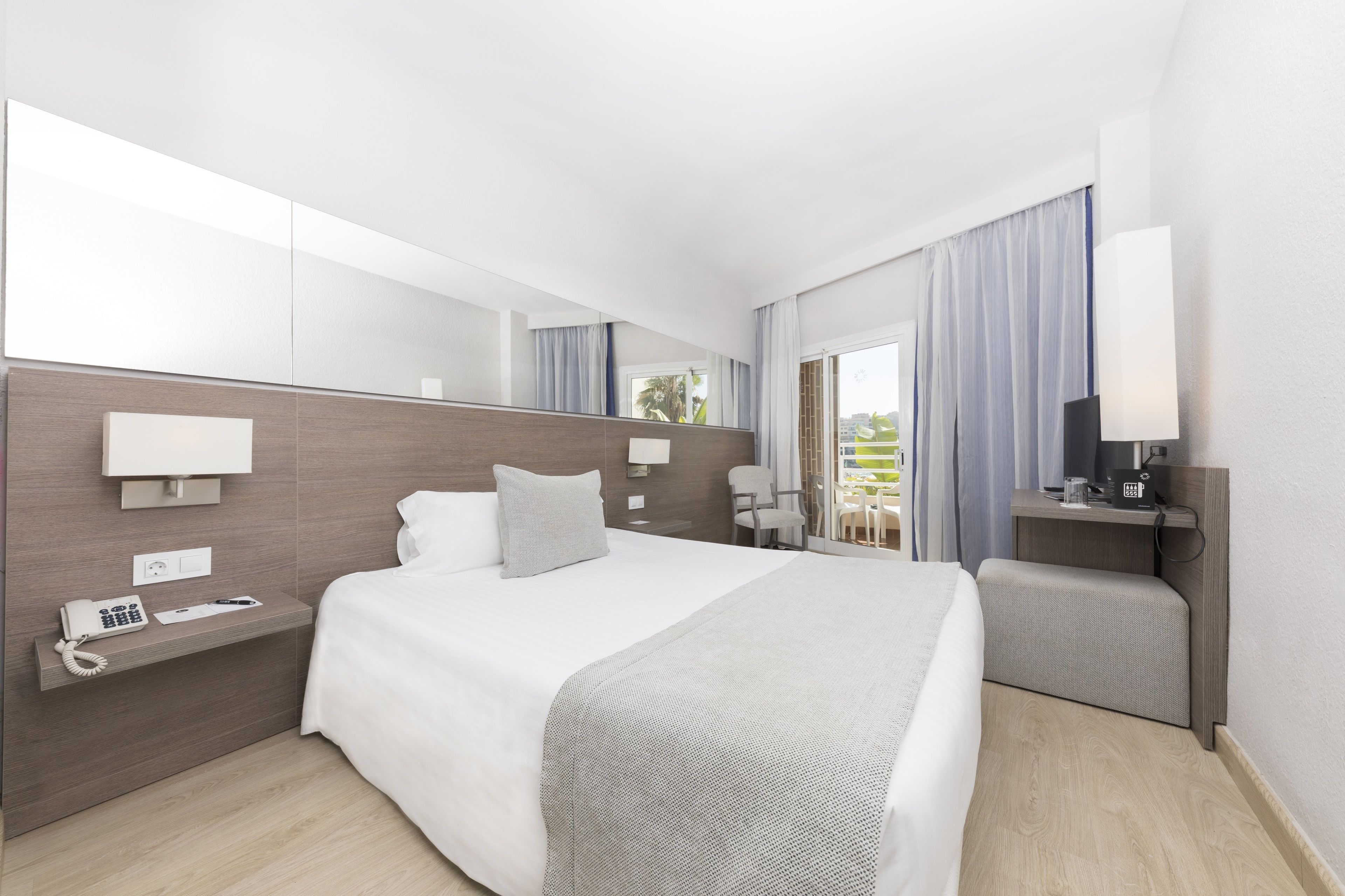 Quarto de hotel moderno com uma cama grande, mesas de cabeceira, escrivaninha e vista para o exterior.