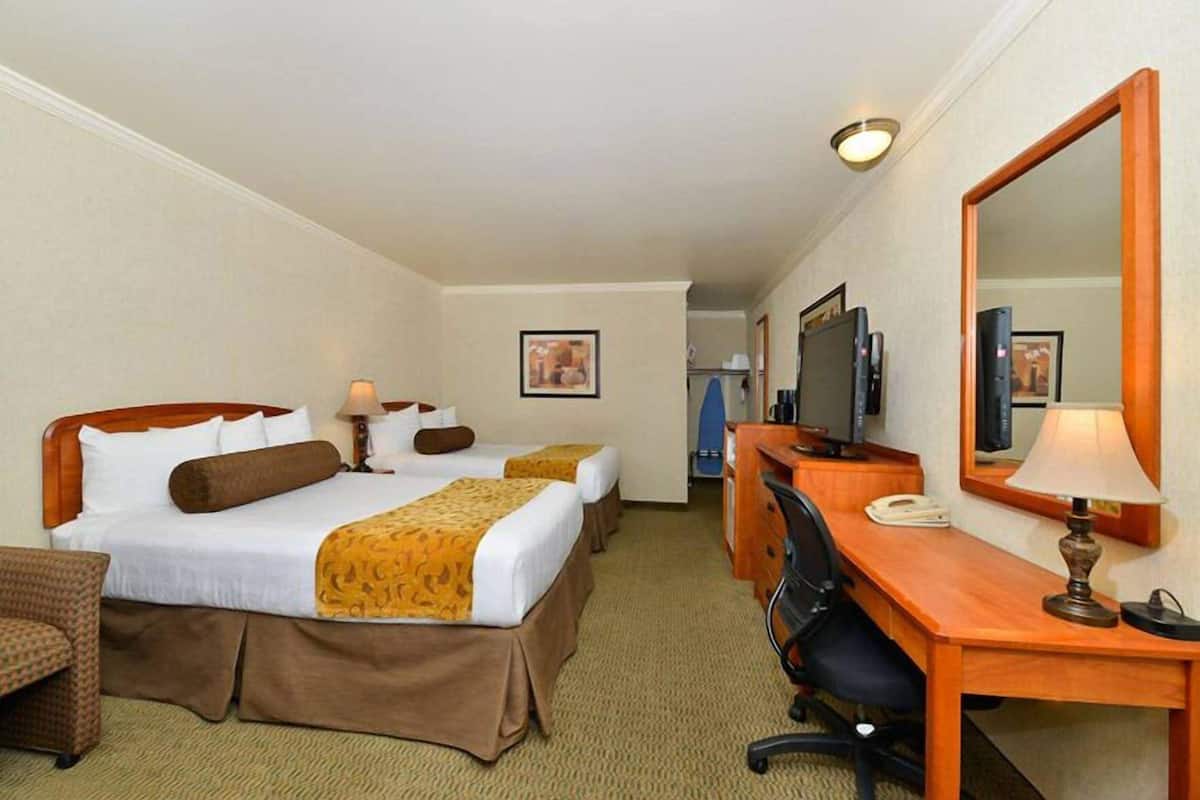 Quarto de hotel com duas camas, uma escrivaninha, uma cadeira, uma televisão e um espelho.