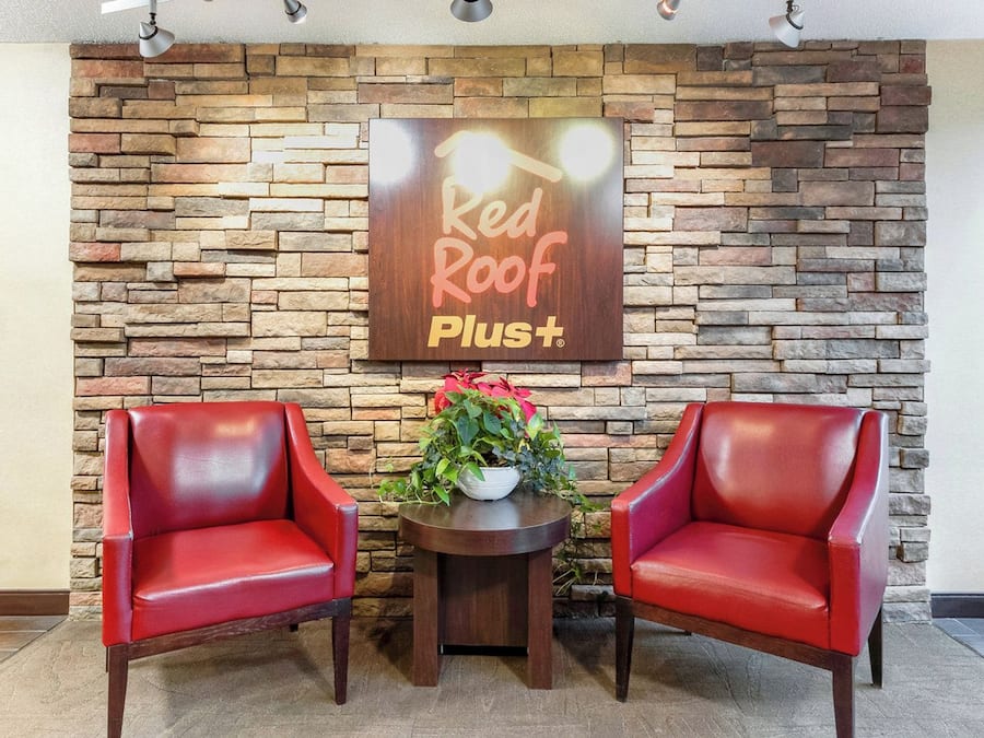 Placa Red Roof Plus, duas poltronas de couro vermelho e uma pequena mesa com um vaso de planta.