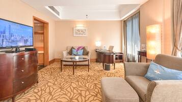Quarto de hotel com uma televisão de tela plana grande, um sofá, uma cadeira, uma mesinha e um abajur.