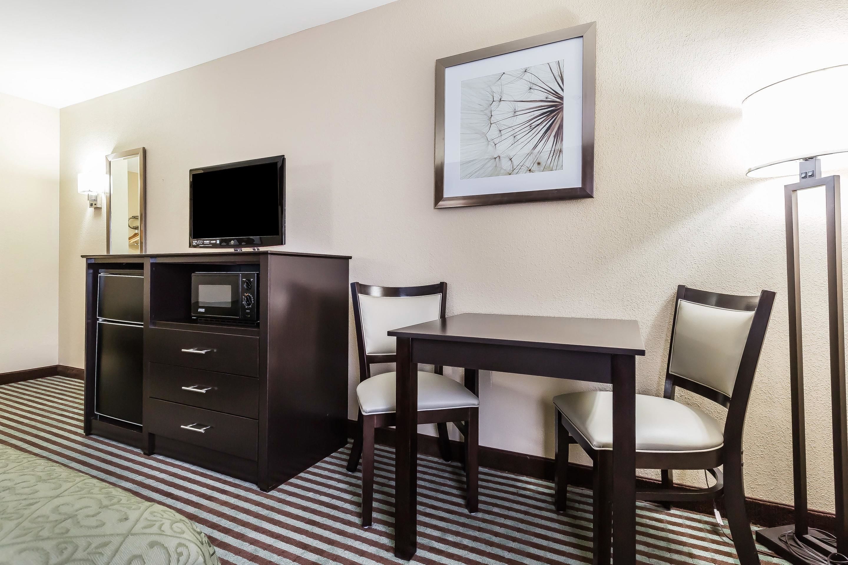 Quarto de hotel com uma mesa de jantar, duas cadeiras, uma TV, micro-ondas e frigorífico.