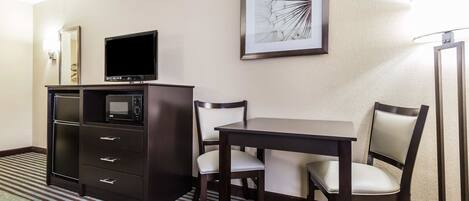 Quarto de hotel com uma mesa de jantar, duas cadeiras, uma TV, micro-ondas e frigorífico.