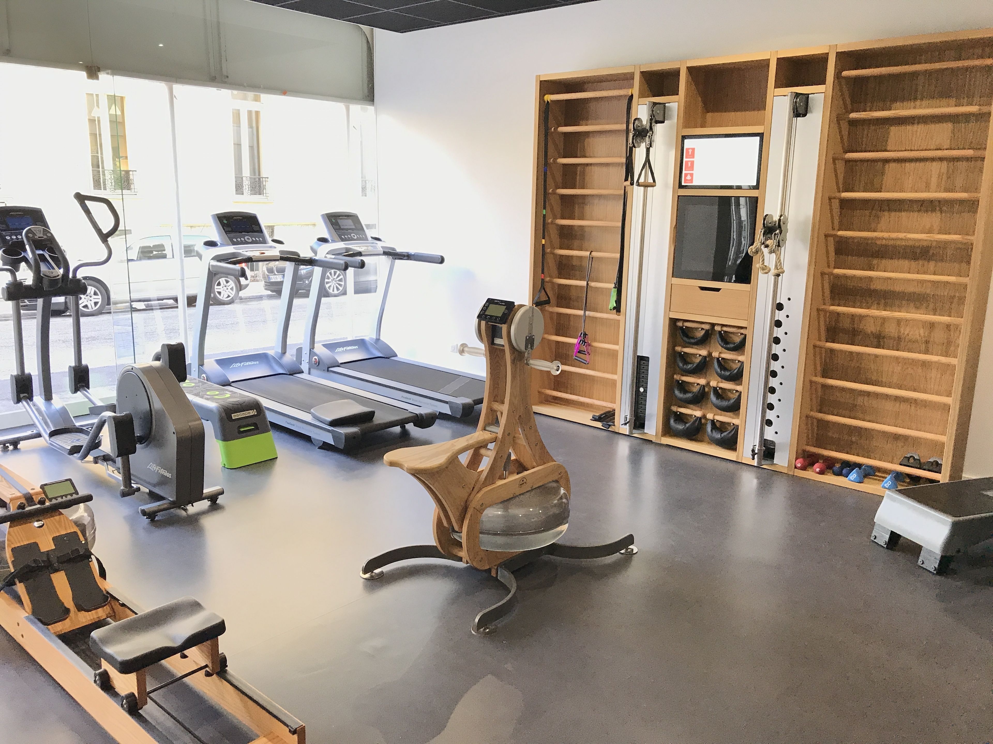 Uma academia com esteiras, remo e um banco de musculação.