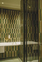 Um banheiro com parede de azulejos xadrez, chuveiro com box de vidro e pia branca com torneira dourada.