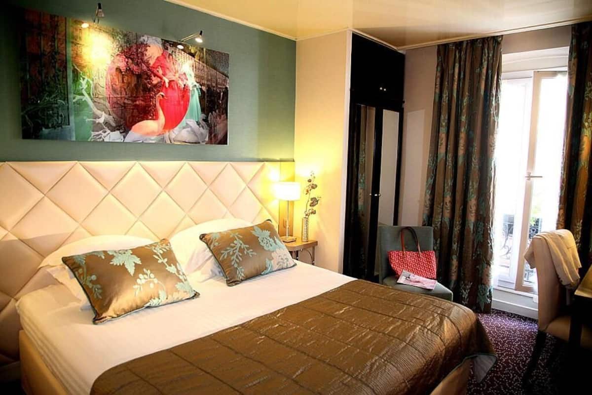 Quarto de hotel com cama, um quadro na parede, mesa de cabeceira, cadeira e vista pela janela.