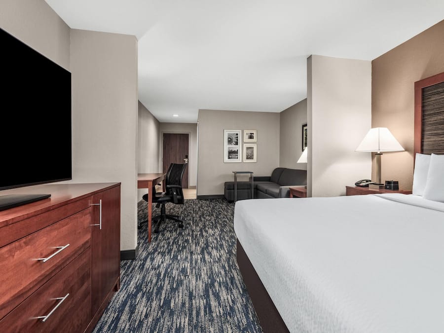 Quarto de hotel com cama, televisão, escrivaninha, cadeira e luminária.