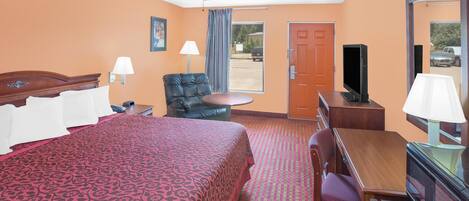 Quarto de hotel com cama, escrivaninha, cadeira, televisão, ventoinha no teto e uma porta.