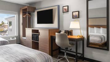 Quarto de hotel com cama, escrivaninha com cadeira, televisão, guarda-roupa e espelho.