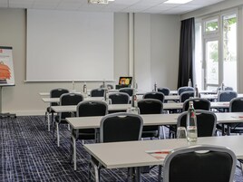 Uma sala de conferências com mesas, cadeiras, tela de projetor e tela para apresentação.