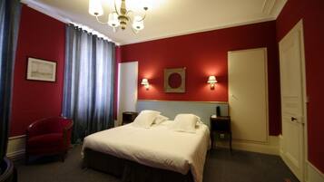 Quarto de hotel com uma cama grande, parede vermelha, lustre e duas luminárias de cabeceira.