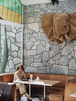 Uma pessoa sentada à mesa, com um muro de pedra e um tapeçário de parede ao fundo.