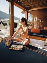 Uma pessoa sentada em um deck com uma mesa de comida, vista para o exterior e uma estrutura de madeira.