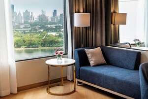 Quarto de hotel moderno com vista para a cidade, um sofá azul, uma mesa redonda dourada e um abajur.