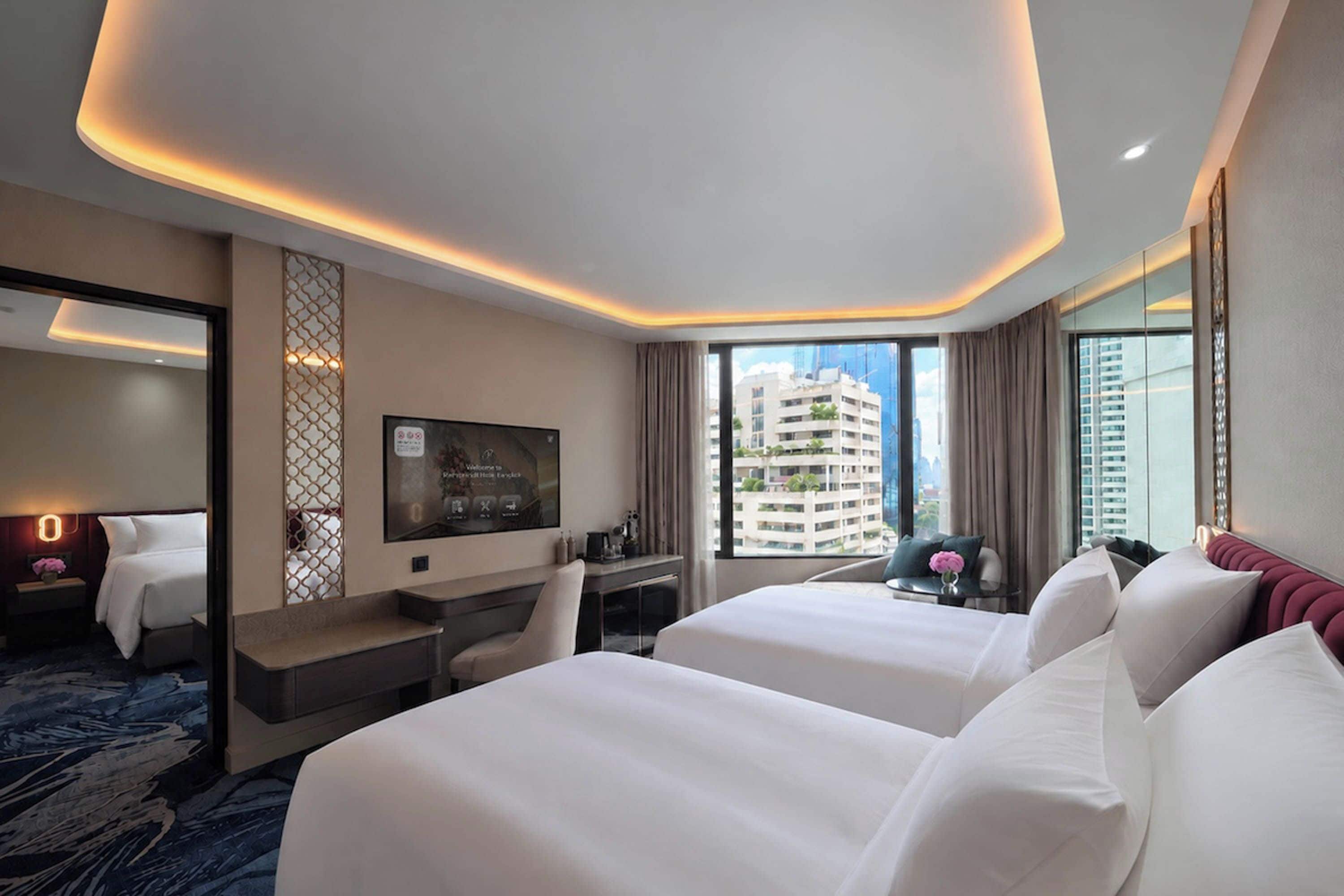 Quarto de hotel com duas camas, uma escrivaninha, televisão e vista para a cidade.