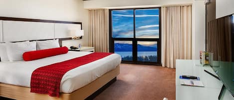Quarto de hotel com uma cama grande, televisão, escrivaninha e janela com vista para a montanha.