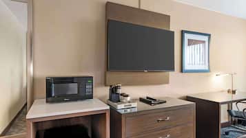 Quarto de hotel com cozinha compacta, televisão de tela plana, cafeteira, escrivaninha com cadeira e quadro decorativo na parede.