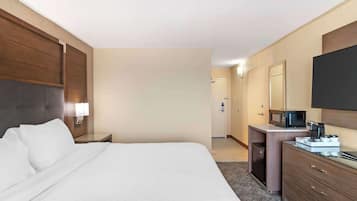 Quarto de hotel com uma cama grande, uma escrivaninha com micro-ondas, cafeteira e espelho.