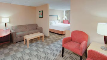 Quarto de hotel com cama, sofá, poltrona, mesa e luminária.