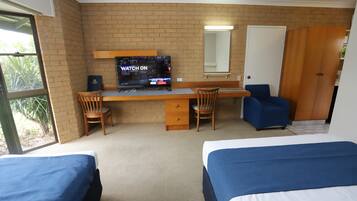 Quarto de hotel com duas camas, uma mesa com televisão, uma cadeira e um guarda-roupa.