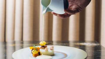 Uma mão despejando um líquido branco sobre um prato com comida e guarnições.