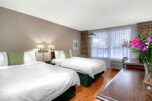Quarto de hotel com duas camas, uma escrivaninha, uma cadeira, um abajur e um vaso com flores.