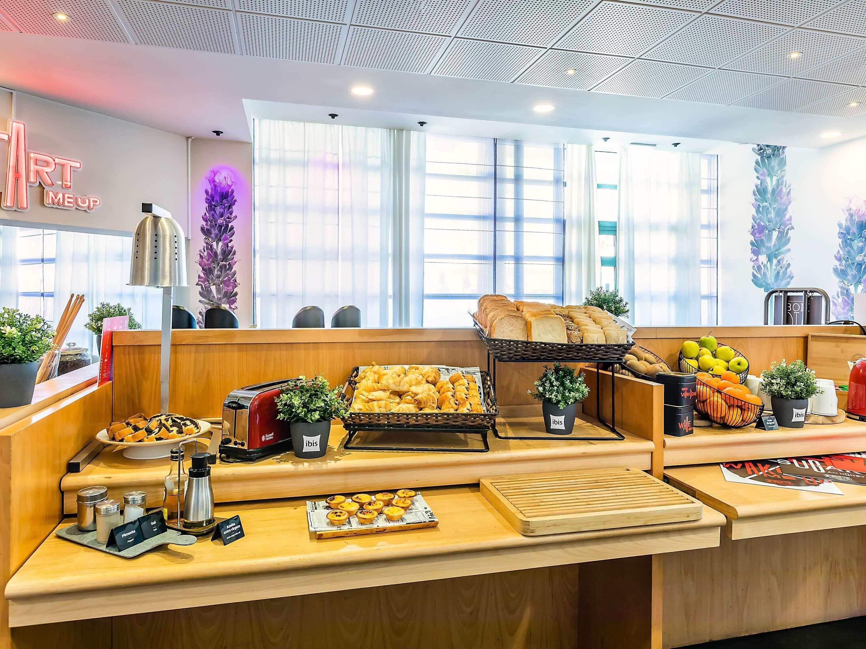 Um buffet de café da manhã com pães, frutas, doces e uma estação de café.