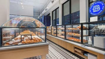 Vitrine de padaria com diversos produtos de panificação em vitrines de vidro, balcão com doces e um letreiro da Paris Baguette Bakery Cafe.