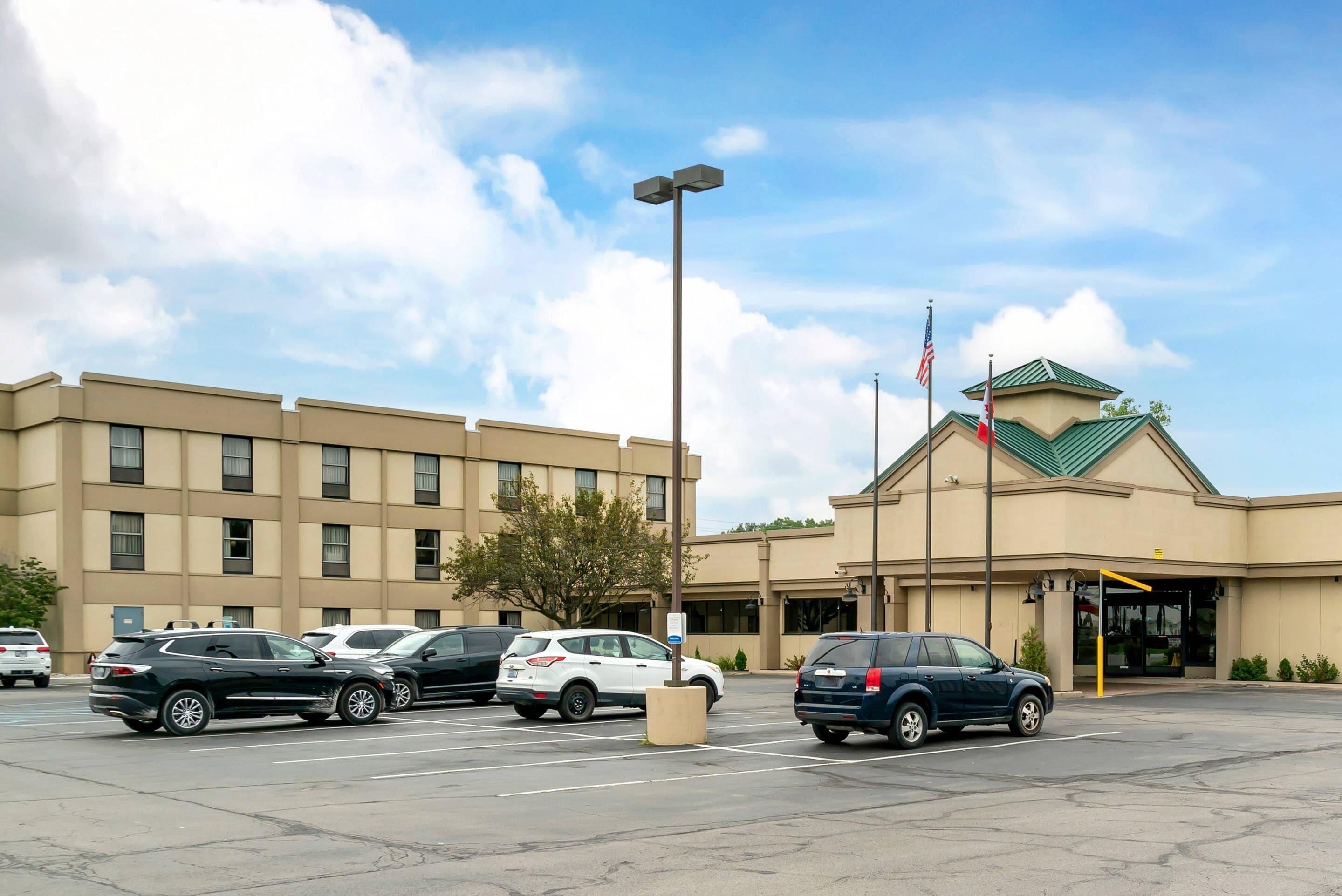 Hotel com estacionamento, vários carros e um edifício com telhado verde e bandeiras americanas.