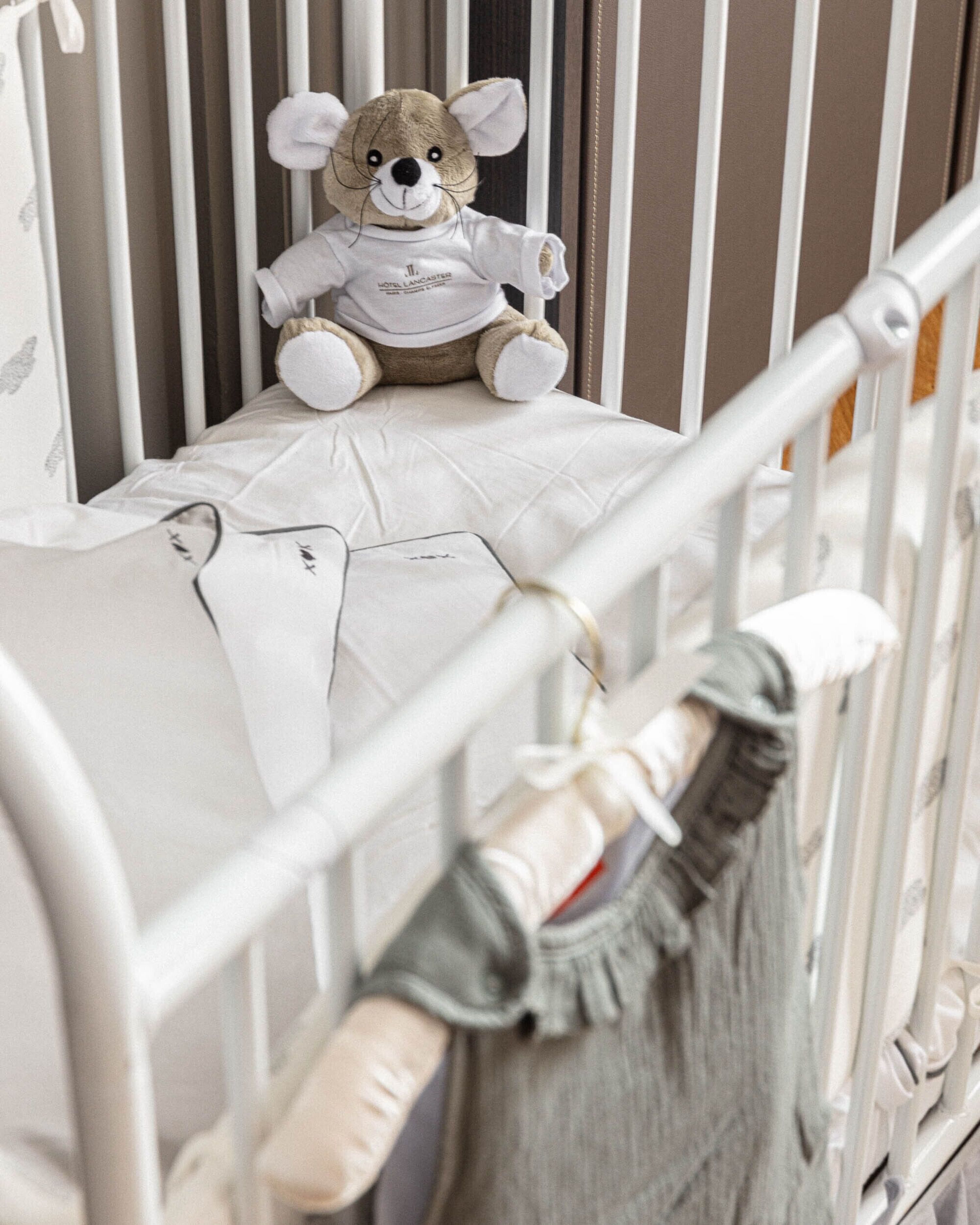 Berço com colchão branco, um urso de pelúcia e uma saia cinza pendurada ao lado.