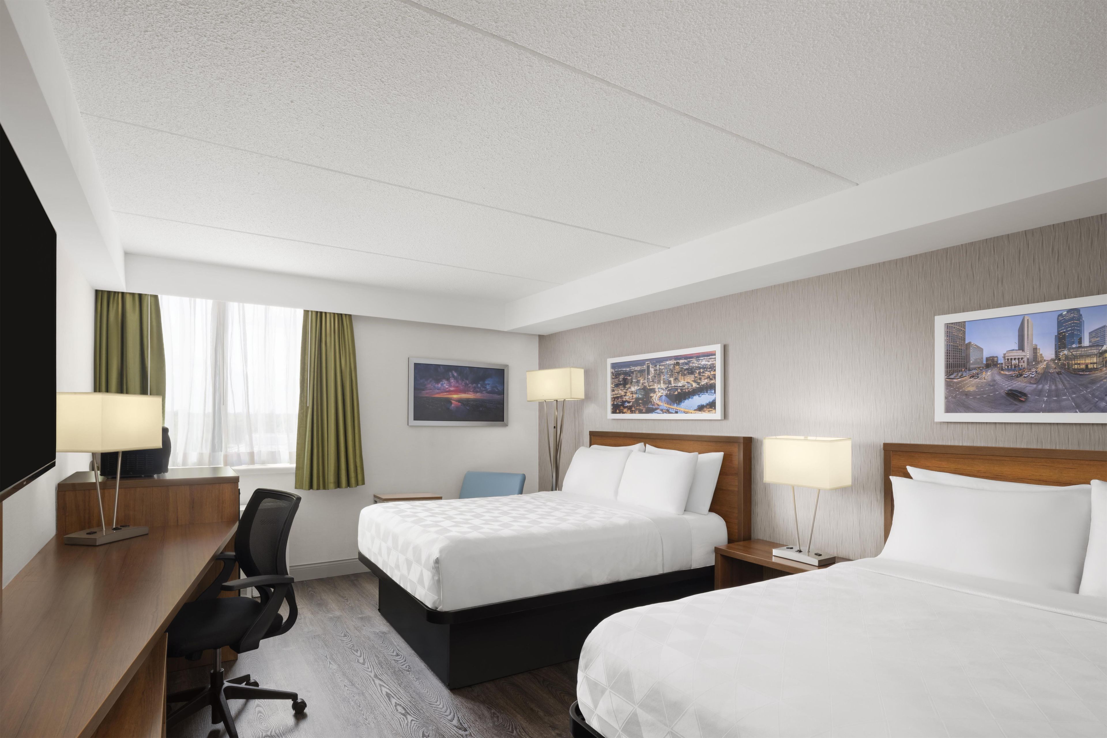 Quarto de hotel com duas camas, uma escrivaninha, uma cadeira e duas luminárias.