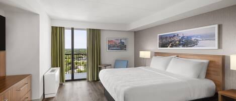 Quarto de hotel com cama, escrivaninha, cadeira, televisão e janela com cortinas.